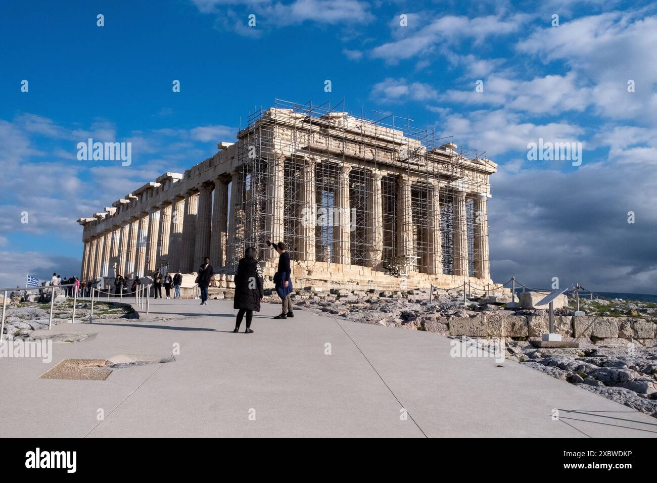 A tourist in front of the Parthenon temple with a facade under construction with scaffolding on ...