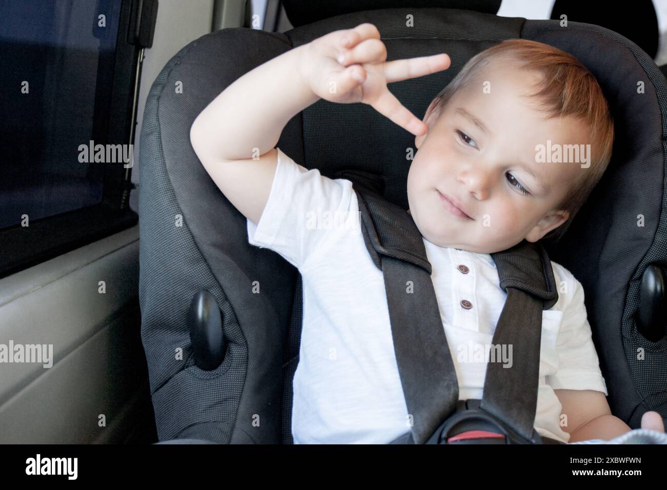 Little boy sitting in a car seat in the car making the victory hand ...