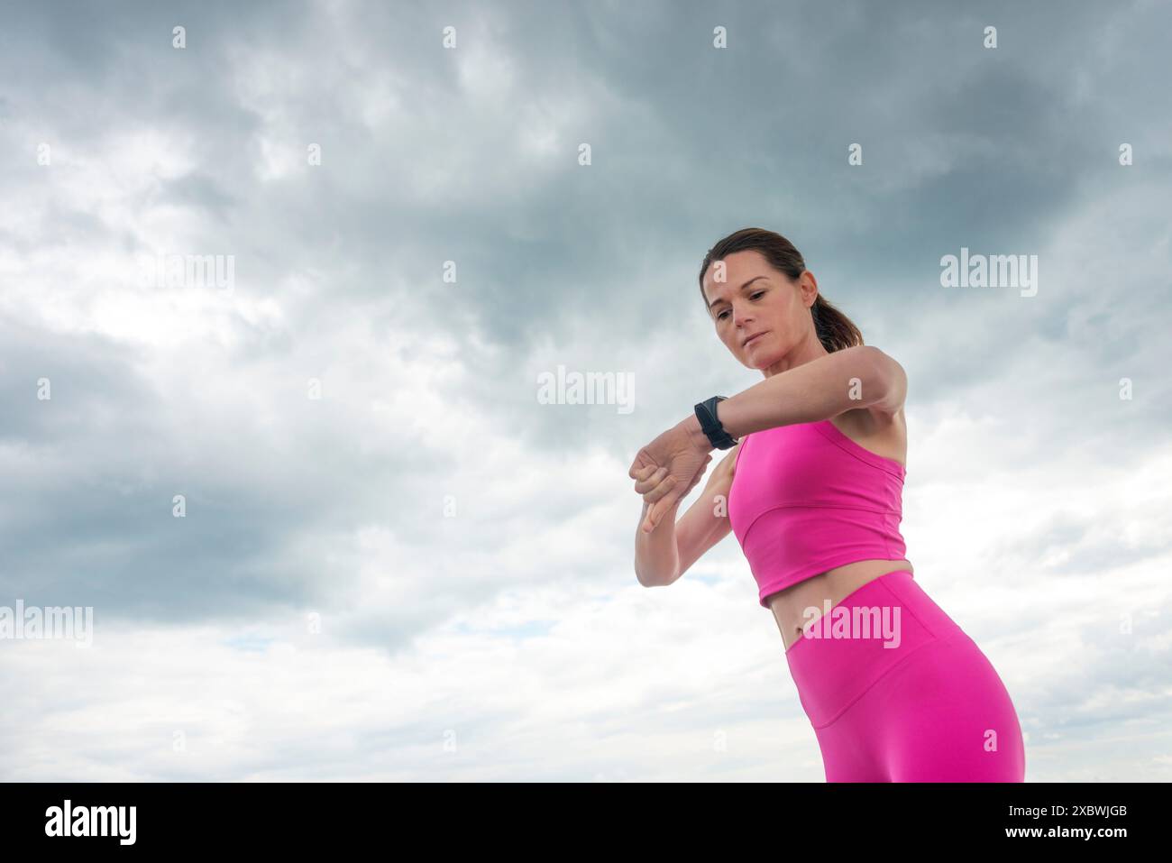 Sporty woman checking her fitness tracker watch, wearing pink sports ...