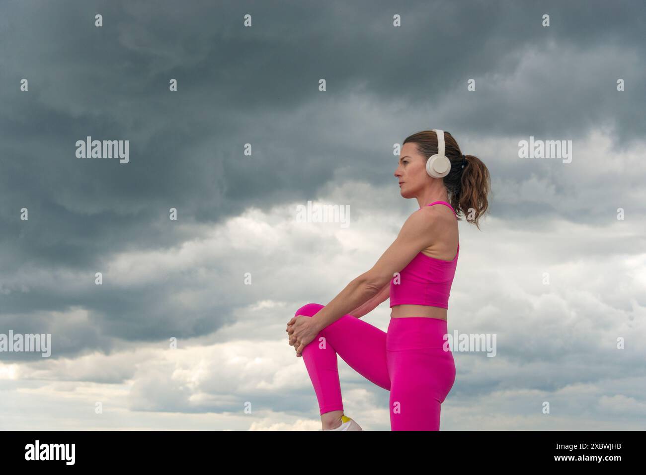 Sporty woman doing leg stretching exercises by water wearing pink ...