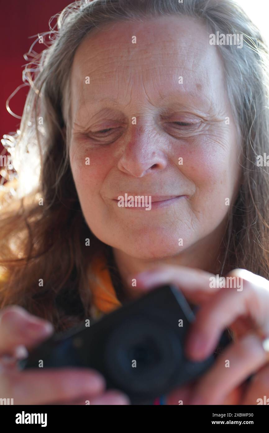 Smiling senior woman with loose hair looks at the back screen of a ...