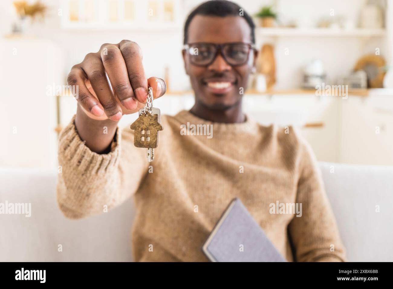 Smiling African American man sitting indoors, holding set of house keys ...