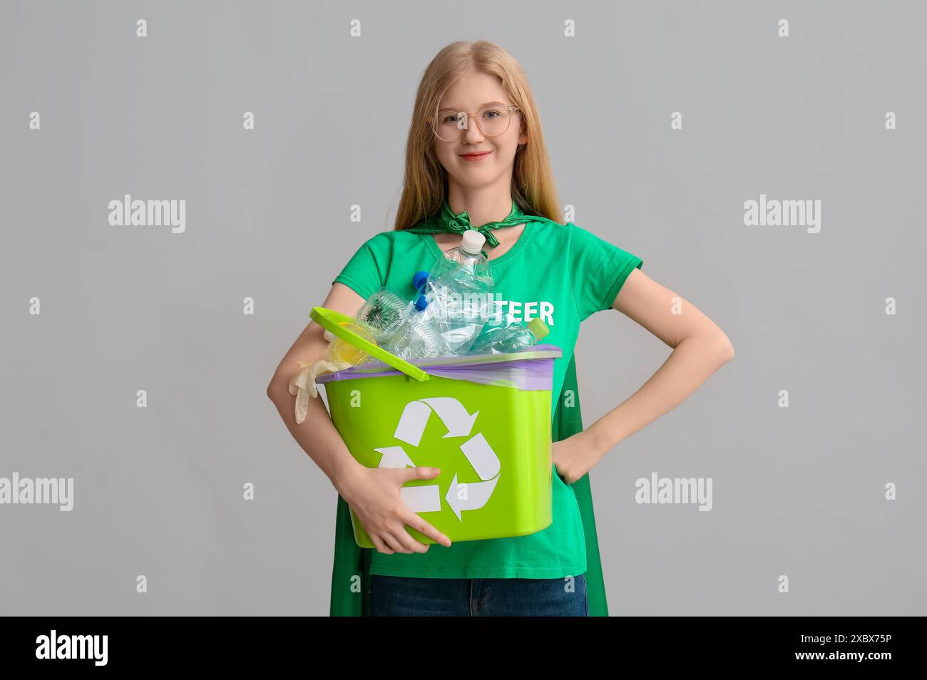 Female volunteer in superhero cape holding recycle bin with plastic on ...