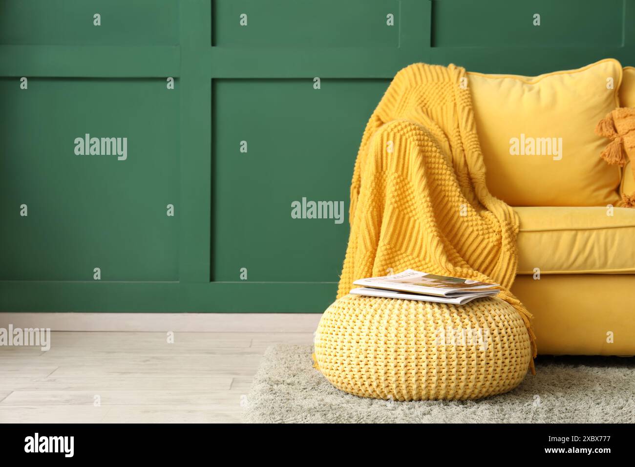 Yellow pouf with magazines and sofa near green wall in living room ...