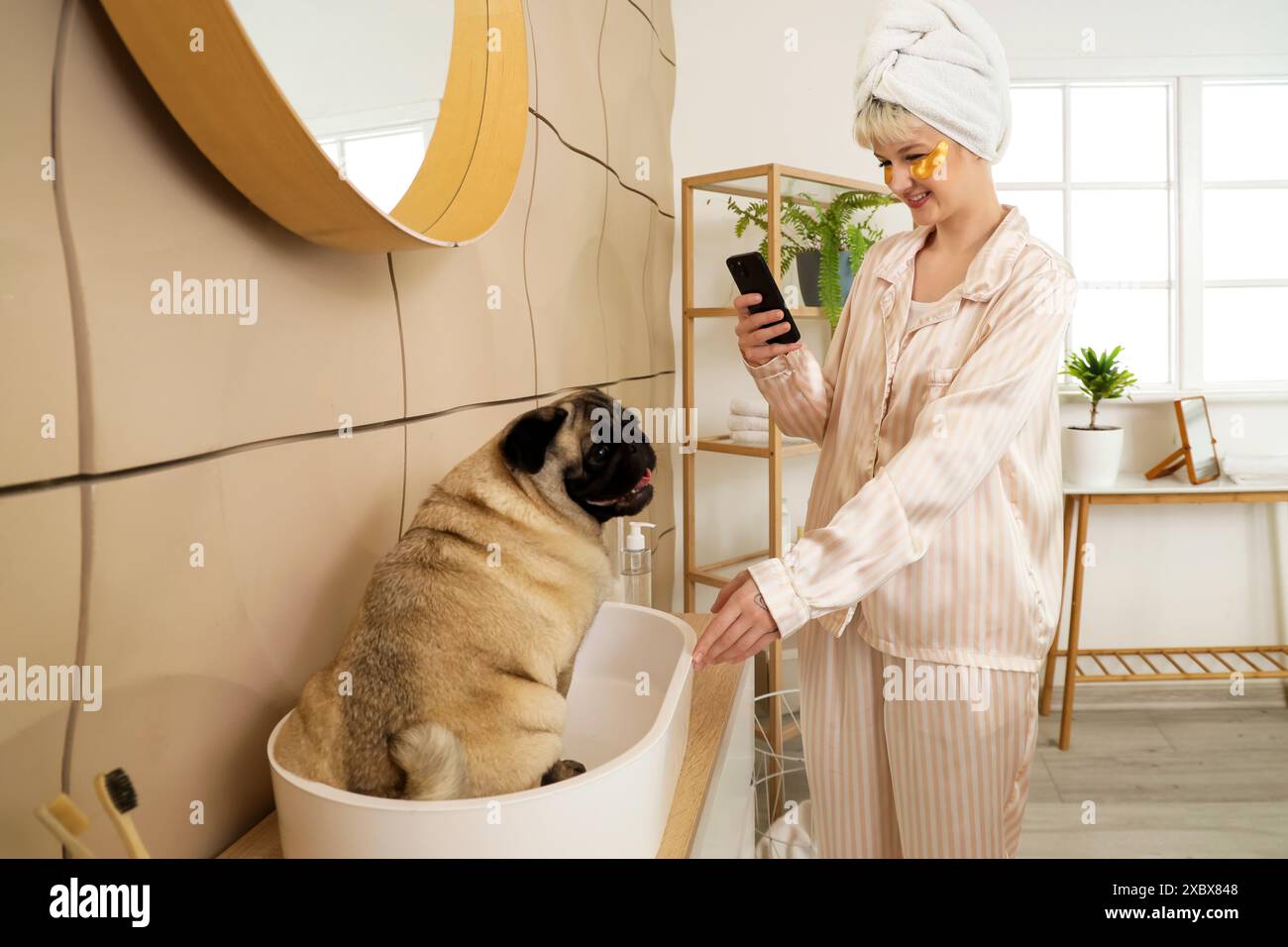 Young woman with under-eye patches taking picture of cute pug dog in ...