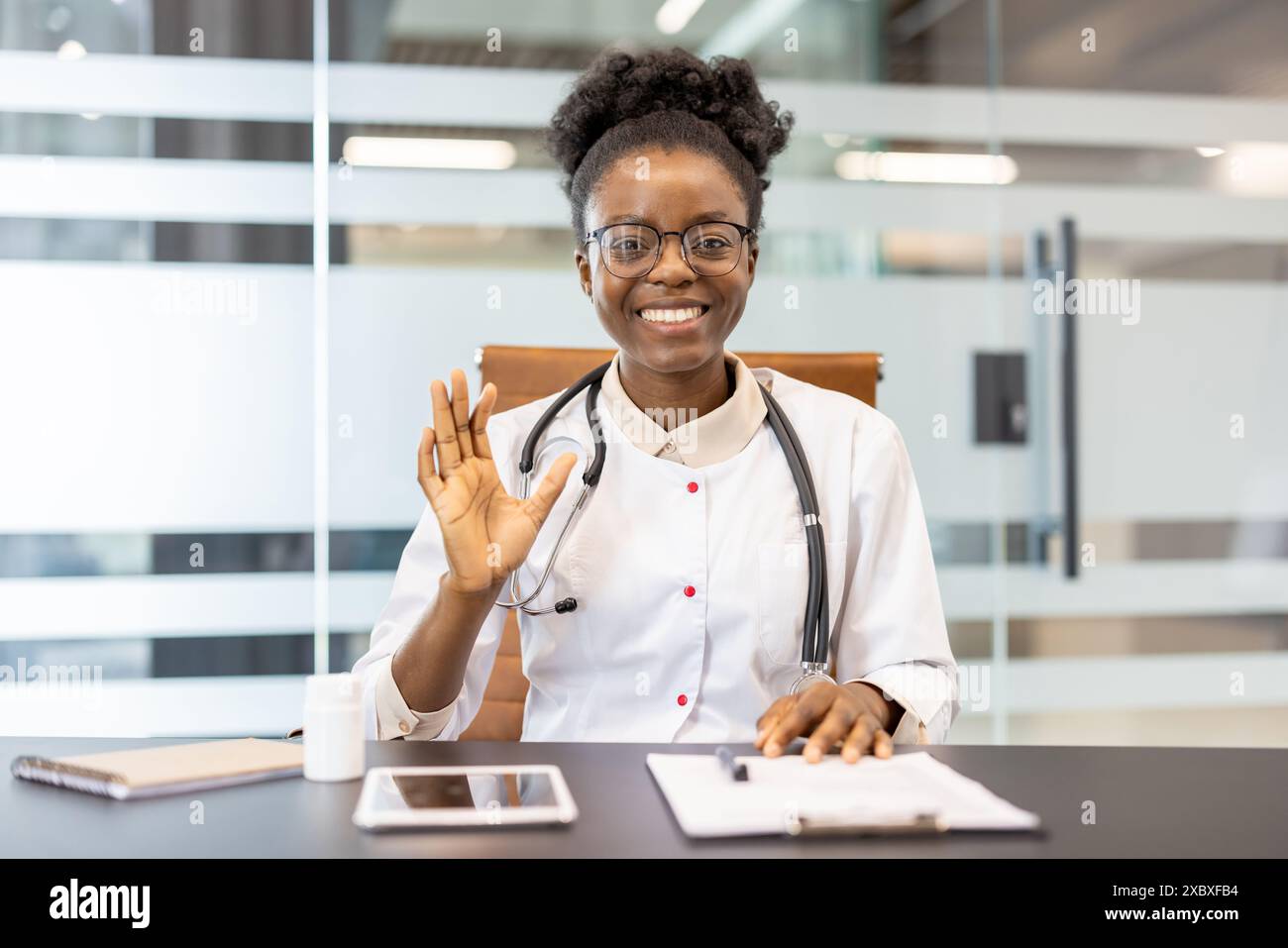 Smiling doctor waving and engaging in online video call in a modern ...