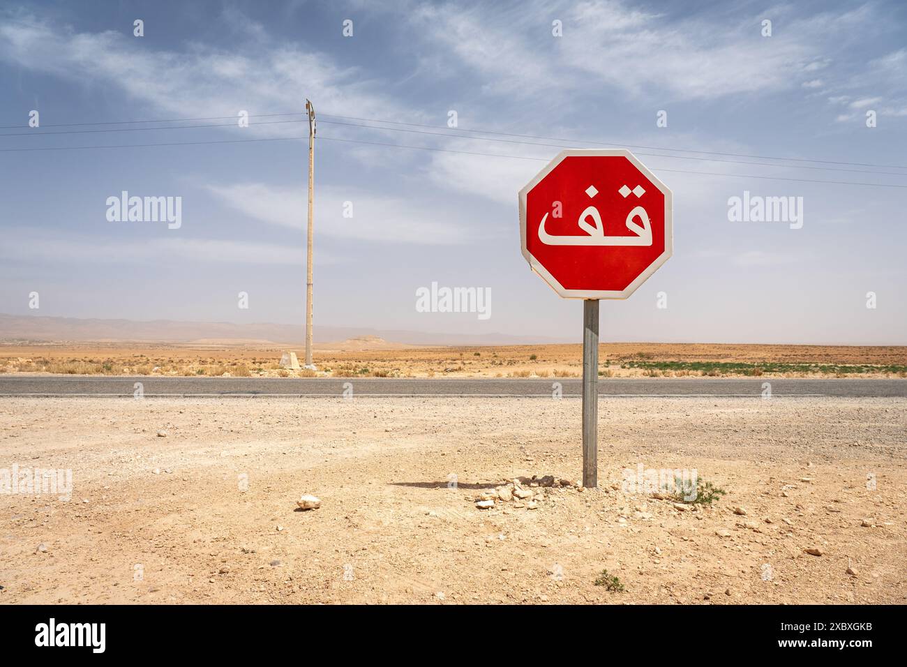 A stop sign with Arabic text in a desert landscape under a clear blue ...