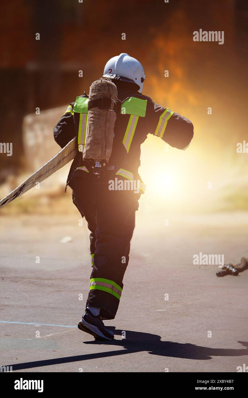 Firefighter with hose running to burning industrial building Stock ...