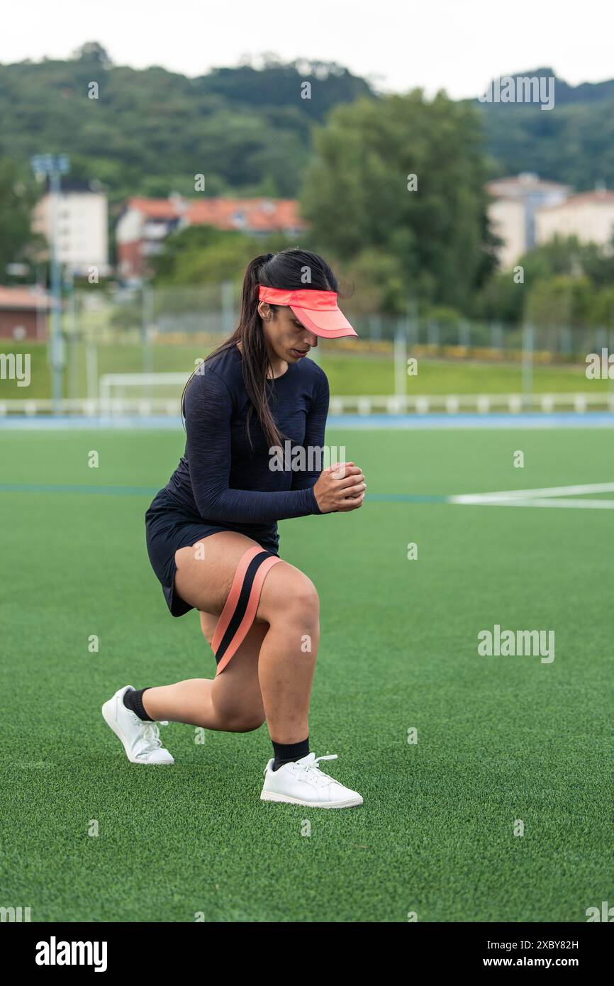 female athlete wearing a cap exercises her legs on soccer field using a ...