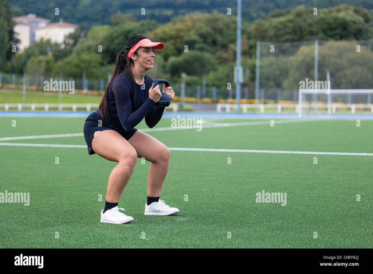 female athlete wearing a cap performs squats while holding a kettlebell ...