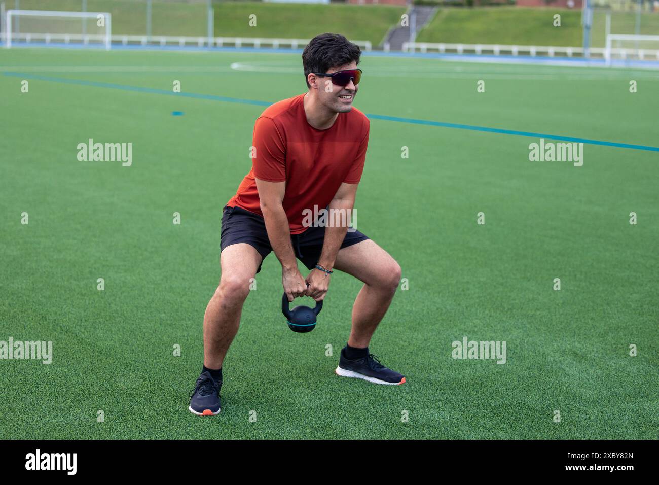 male athlete wearing sunglasses performs squats with a kettlebell ...