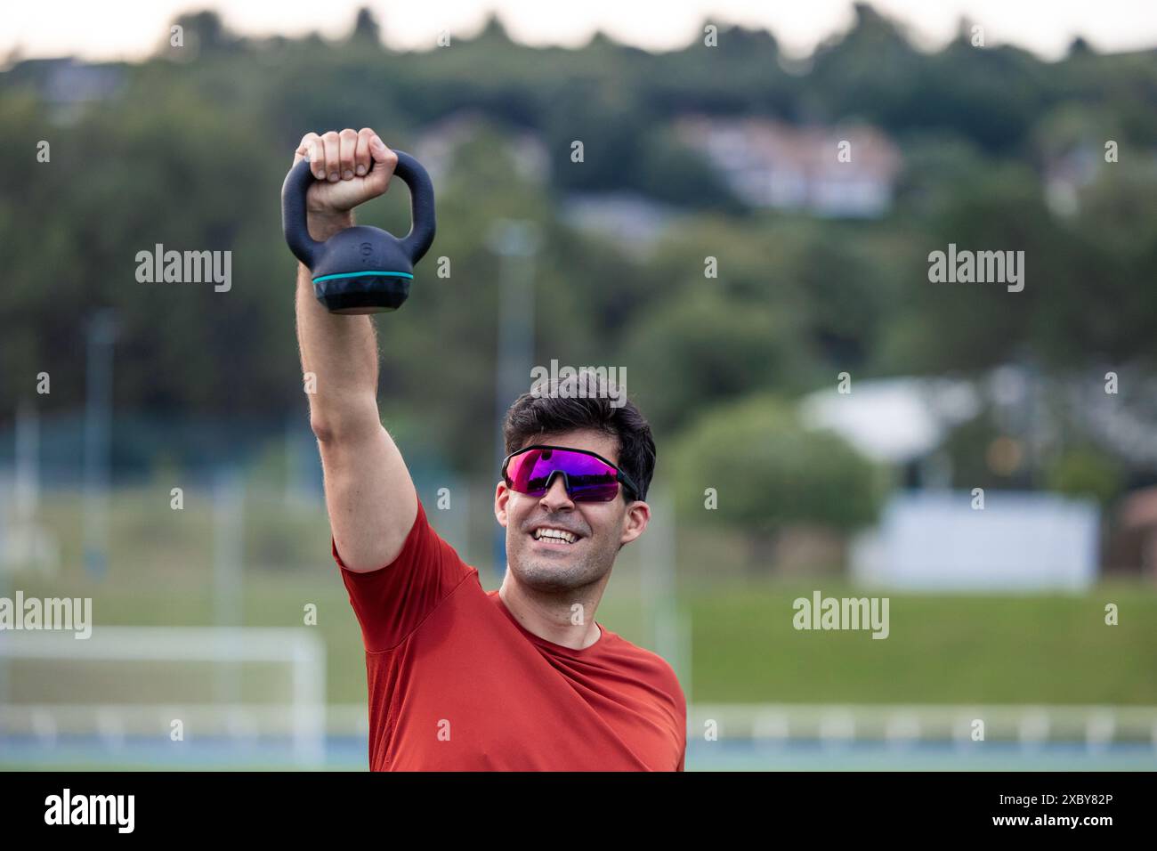 closeup sportsman wearing sunglasses lifts a kettlebell overhead with ...