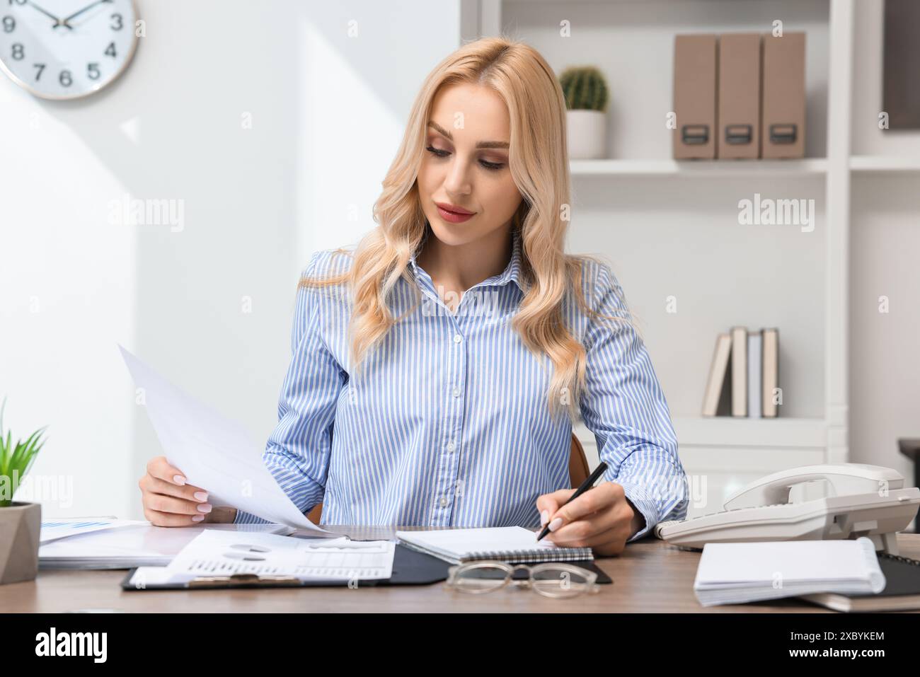 Secretary with document taking notes at table in office Stock Photo - Alamy