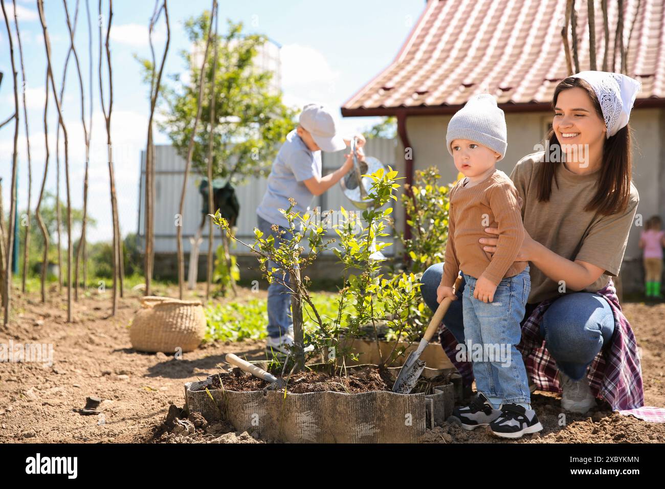 Mother and her children planting tree together in garden Stock Photo ...