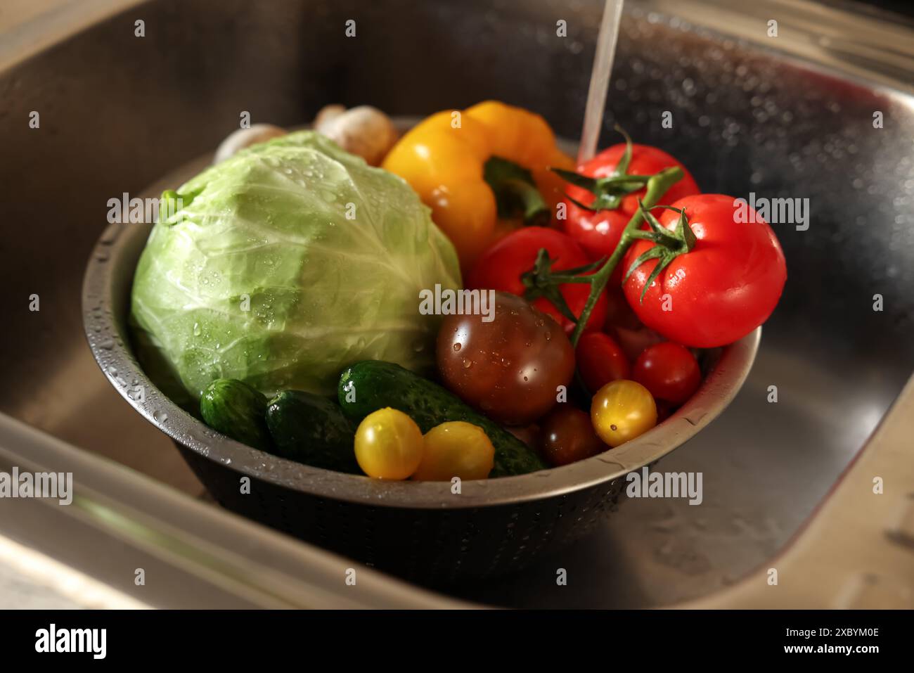 Washing different vegetables with tap water in metal colander inside ...