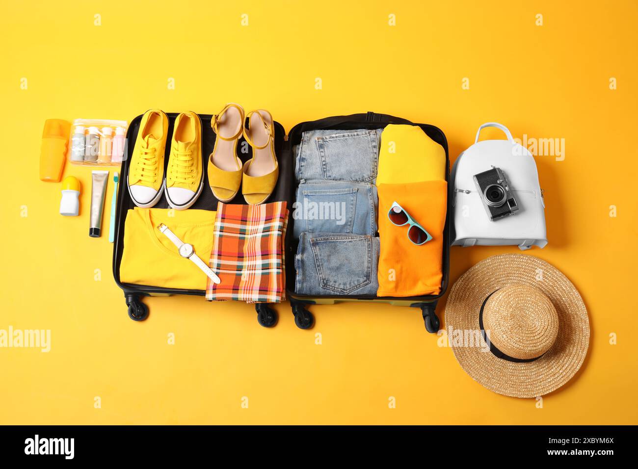 Open suitcase with traveler's belongings on yellow background, flat lay ...