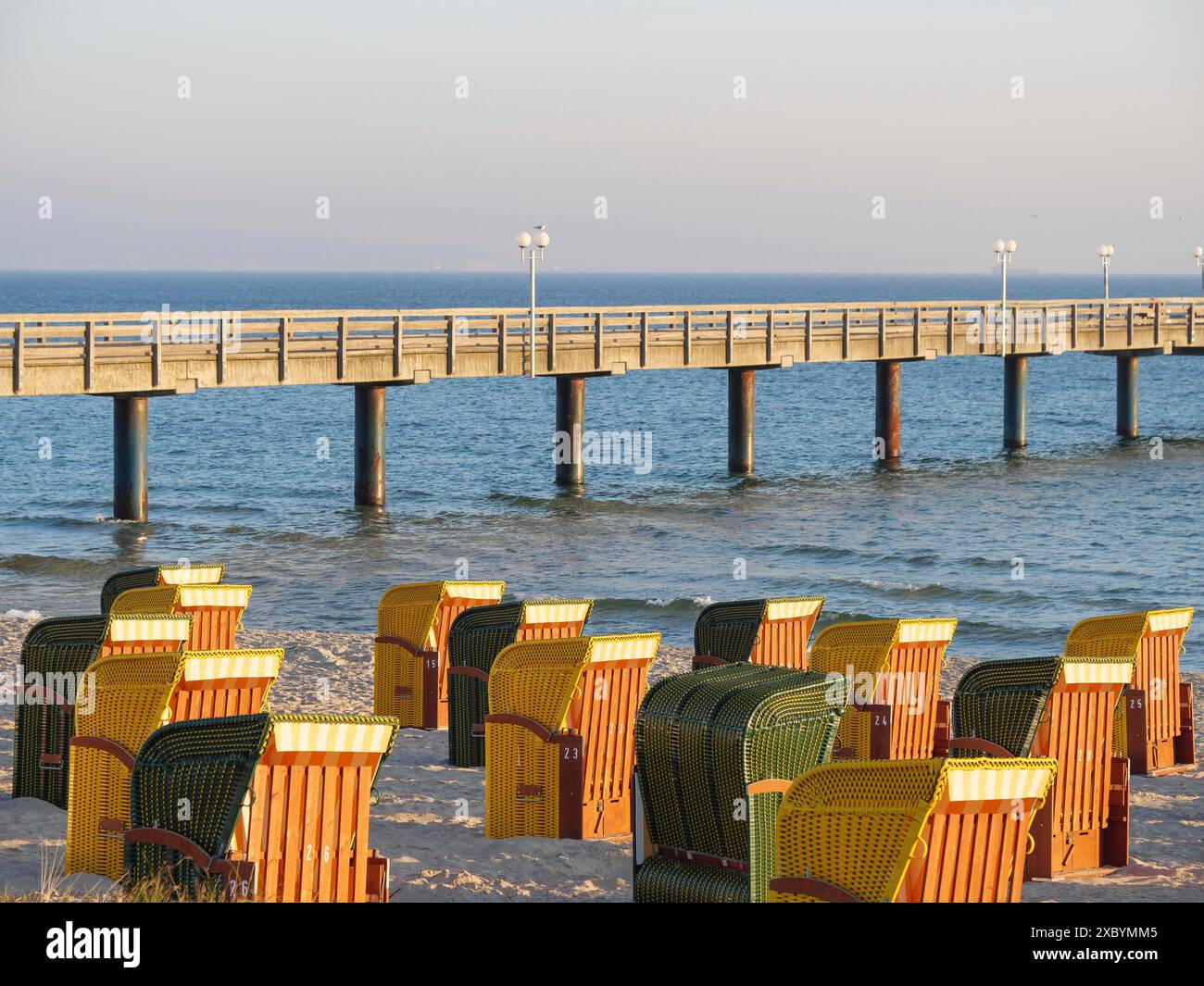 Colourful beach chairs stand on the sandy beach in front of a long ...