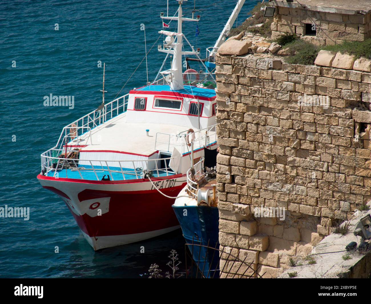 Red ship in blue water next to a stone coastal wall in a harbour area ...