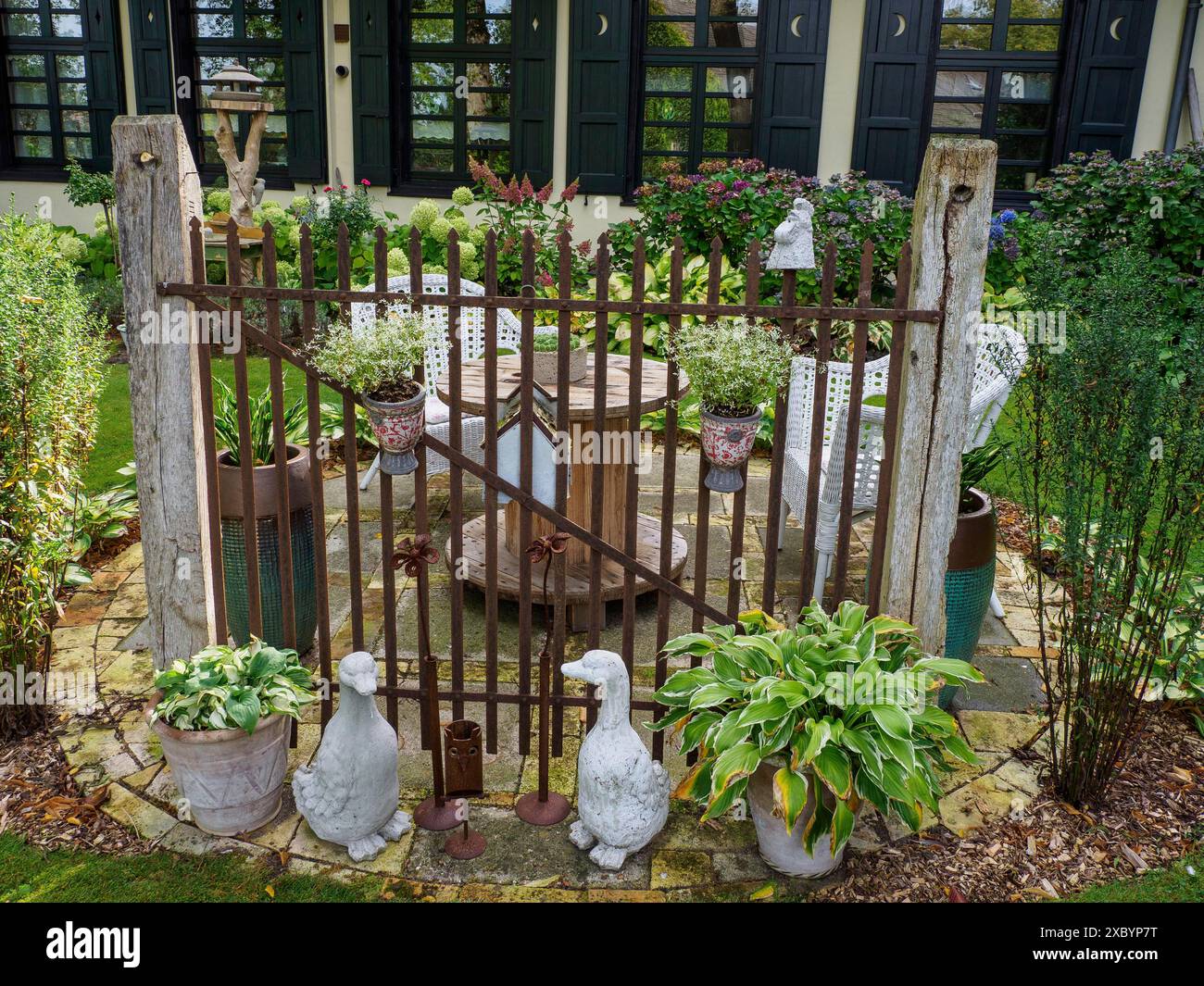 A rustic garden gate with statues and various plants surrounded by ...