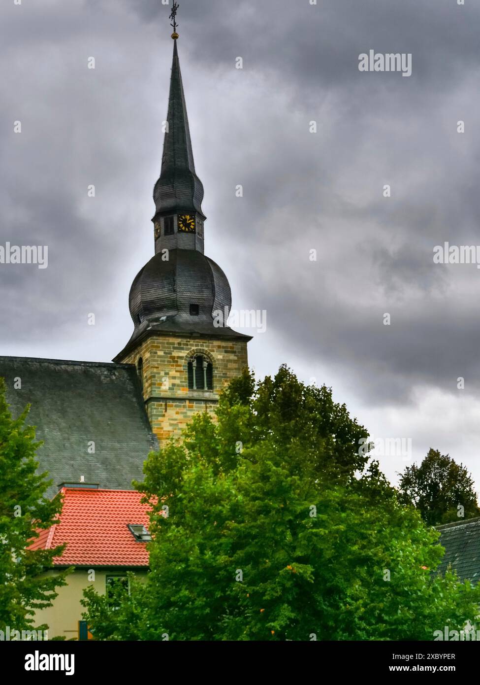 A tall church tower with clock against a dramatic, cloudy sky, Gothic ...