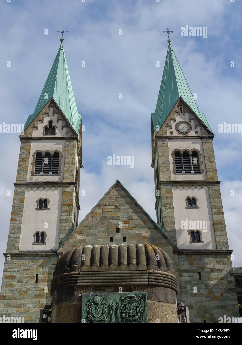 Gothic church with striking towers and a clock in front of a cloudy sky ...