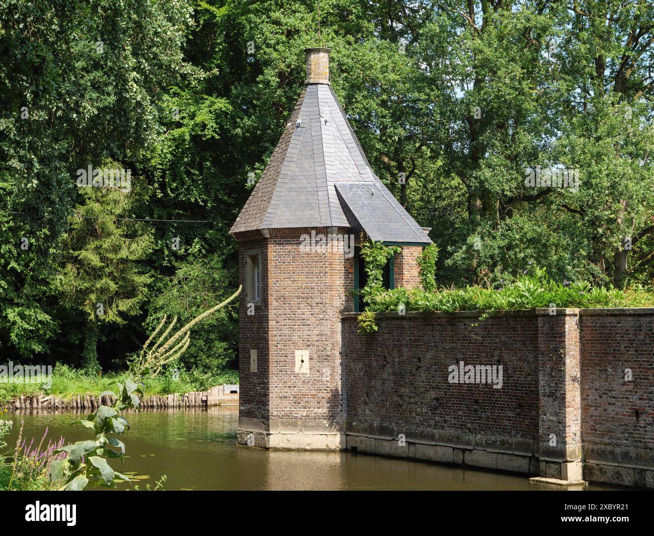 Brick round tower with grey pointed roof on a moat, surrounded by green ...