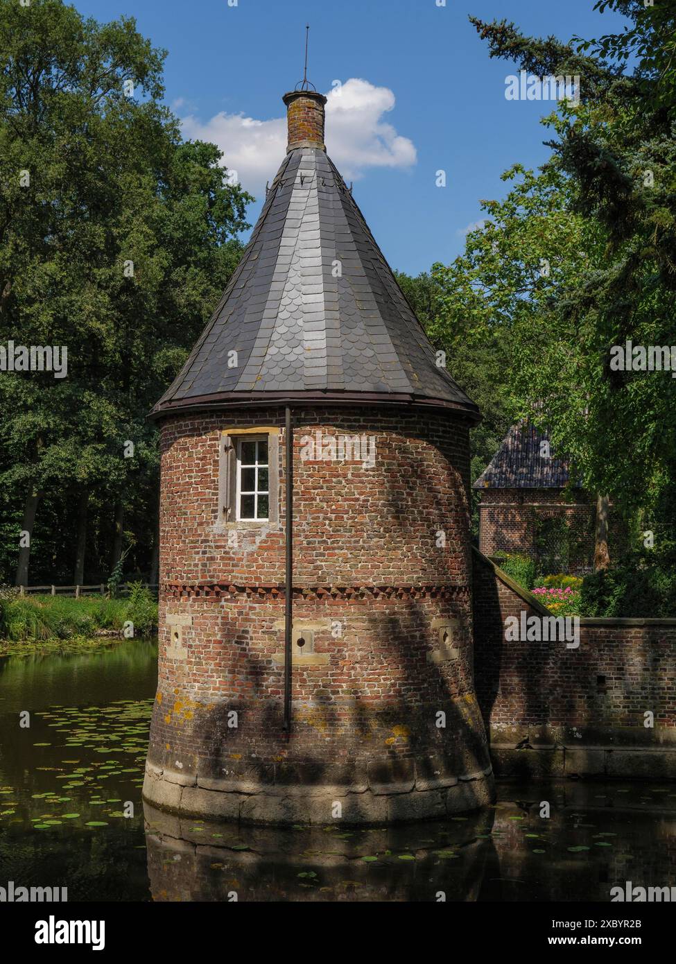 Brick round tower with lead-grey roof on a moat, surrounded by summer ...