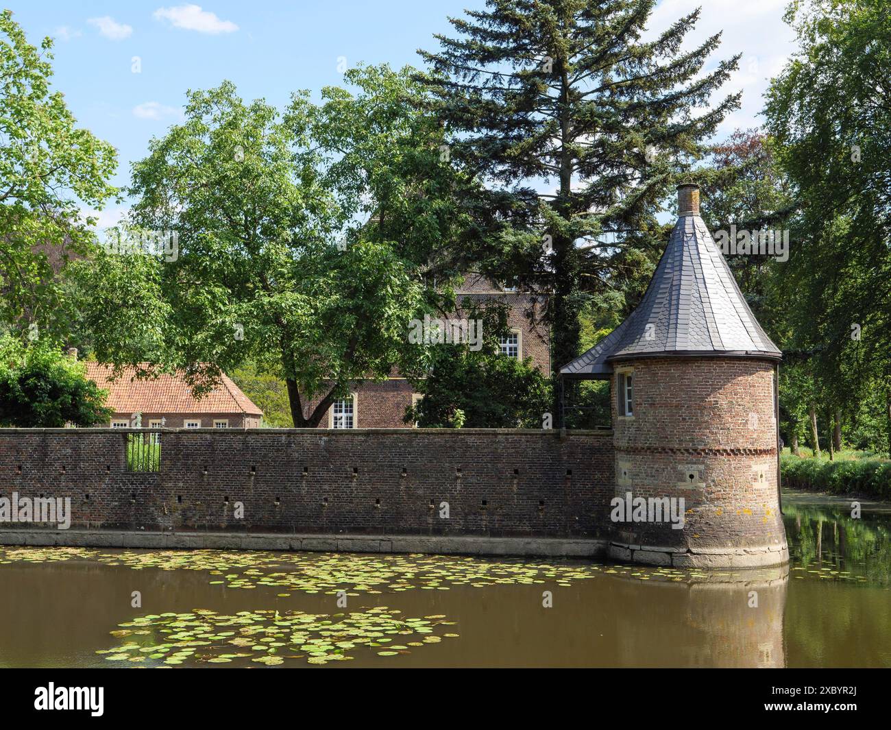 Brick round tower with pointed roof by a moat, surrounded by summer ...
