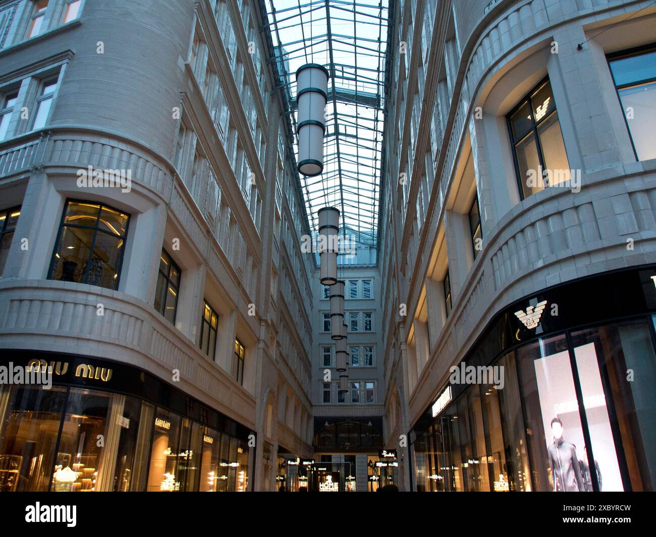 Modern shopping arcade with a glass roof, flanked by shop windows and ...