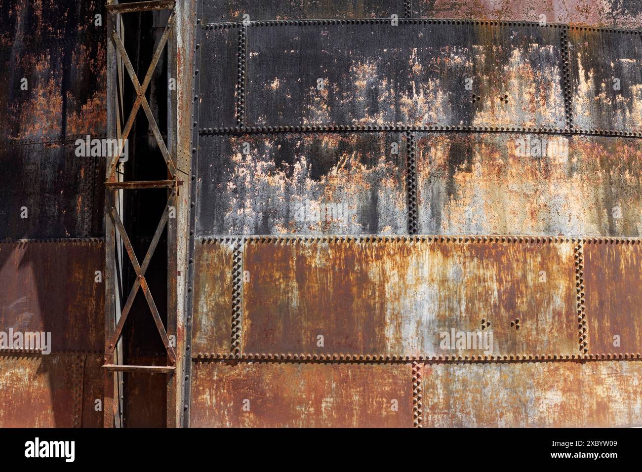 Riveted walls of an old gas storage tank, covered with rust, industrial ...