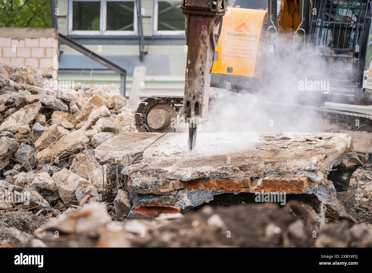 Demolition work on a building with an excavator breaking up concrete. Dust and debris are ...