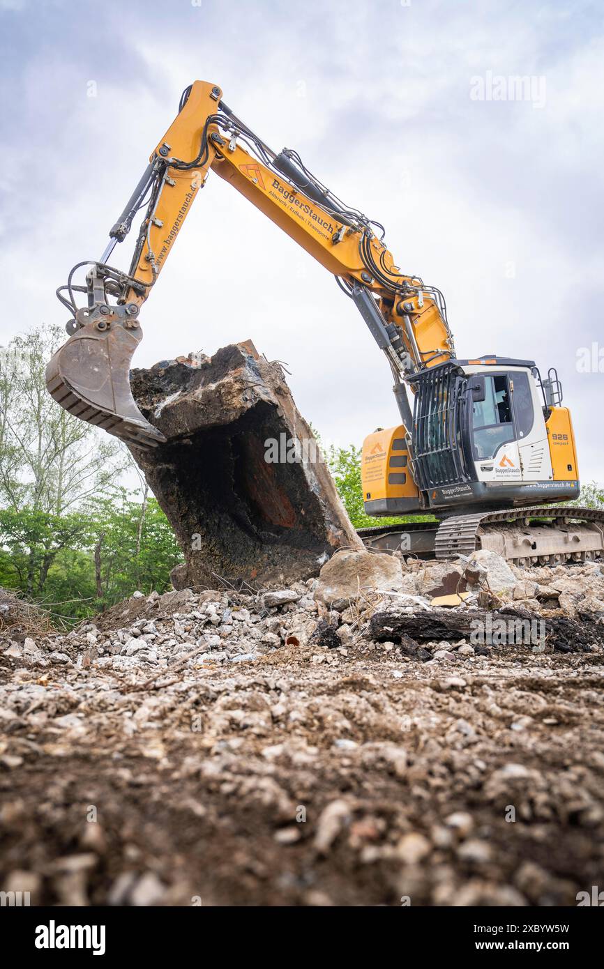 An excavator lifts a large piece of rubble on a building site. The sky ...