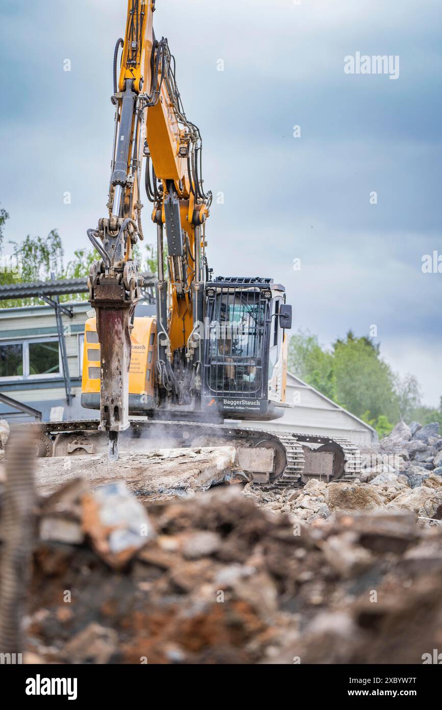 Excavator breaking up concrete on a building site. Debris and dust are ...