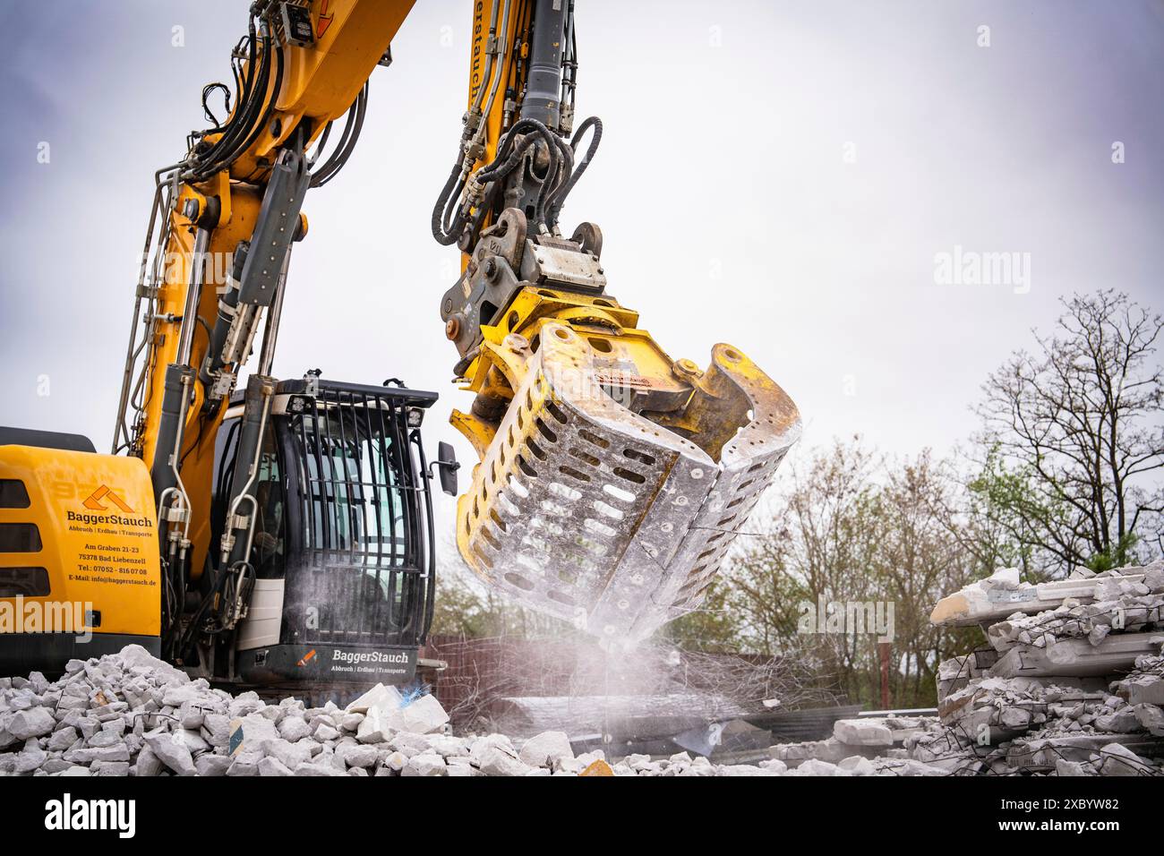 Large excavator with a metal grab crushes building rubble while water ...