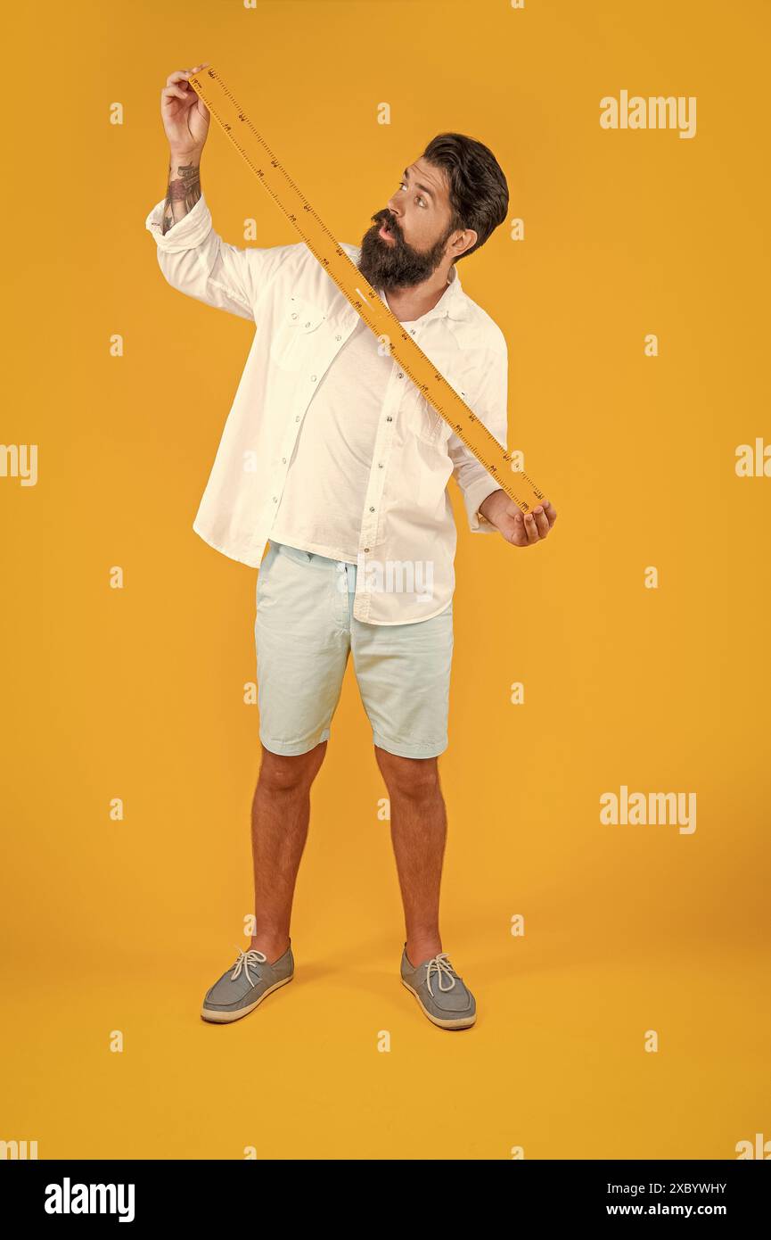 photo of surprised man hold school ruler isolated on yellow background ...