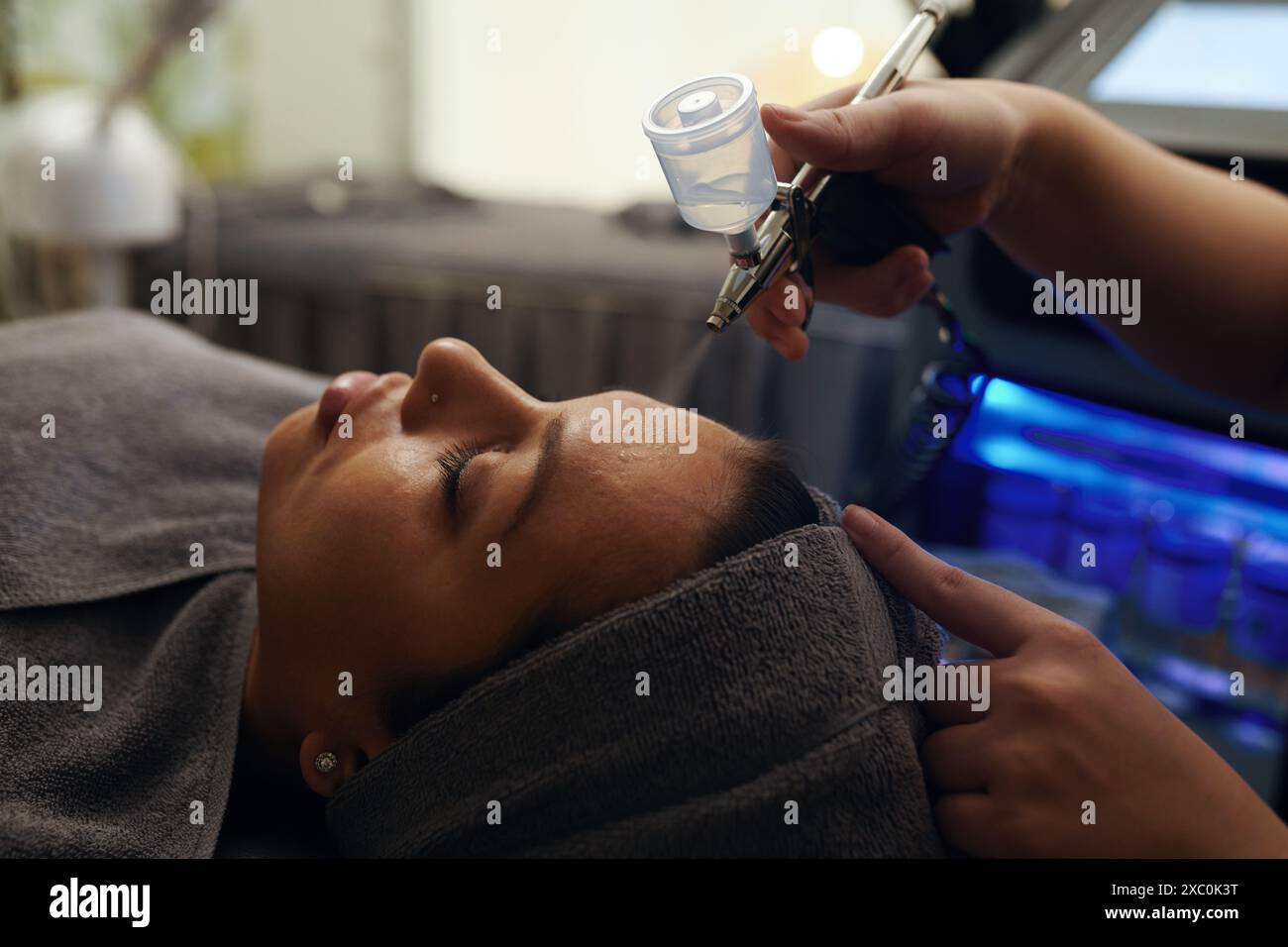 Spraying hydrating emulsion on face of woman after beauty treatment ...