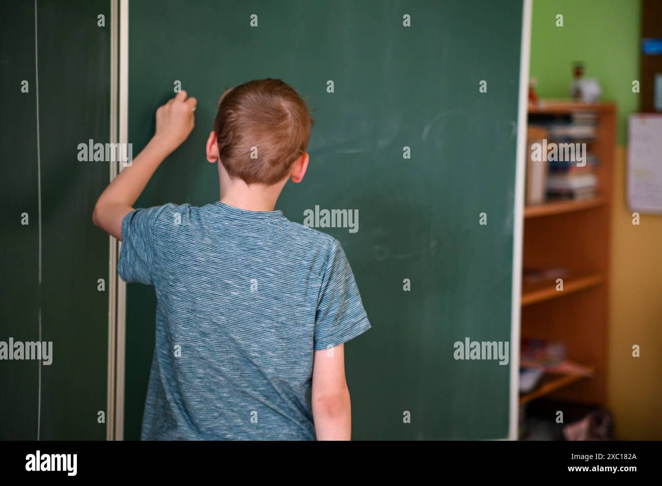 Young student is writing on a large green chalkboard while solving a ...