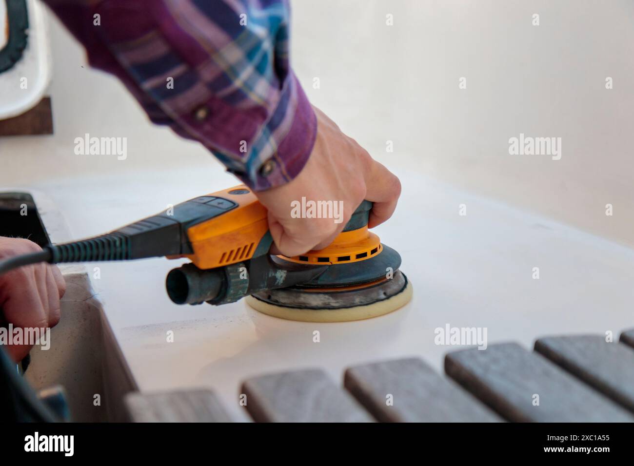 Yacht maintenance. A man polishing white boat by grinder machine in the ...