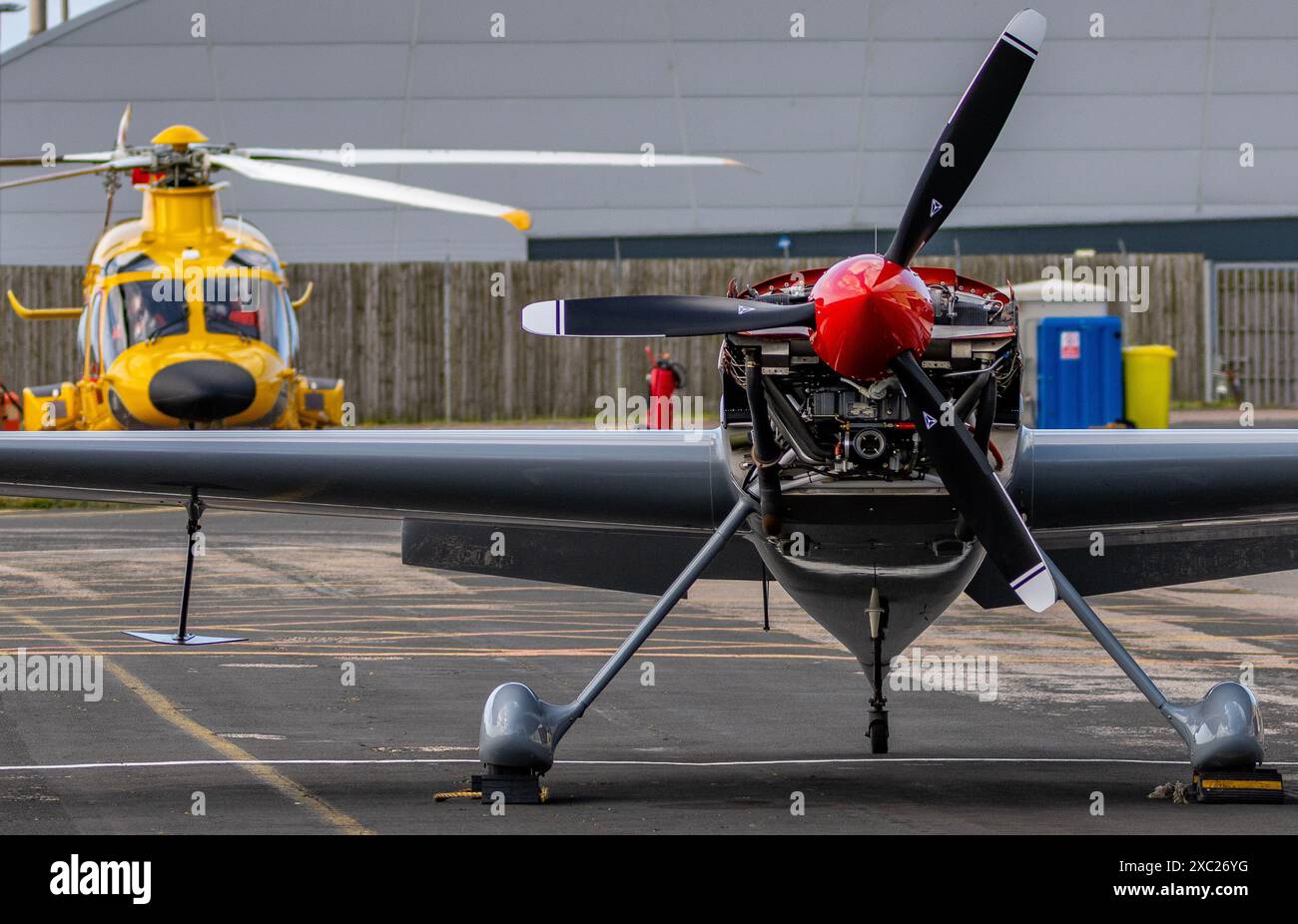 Red nosed aerobatic aircraft parked in front of yellow helicopter Stock ...