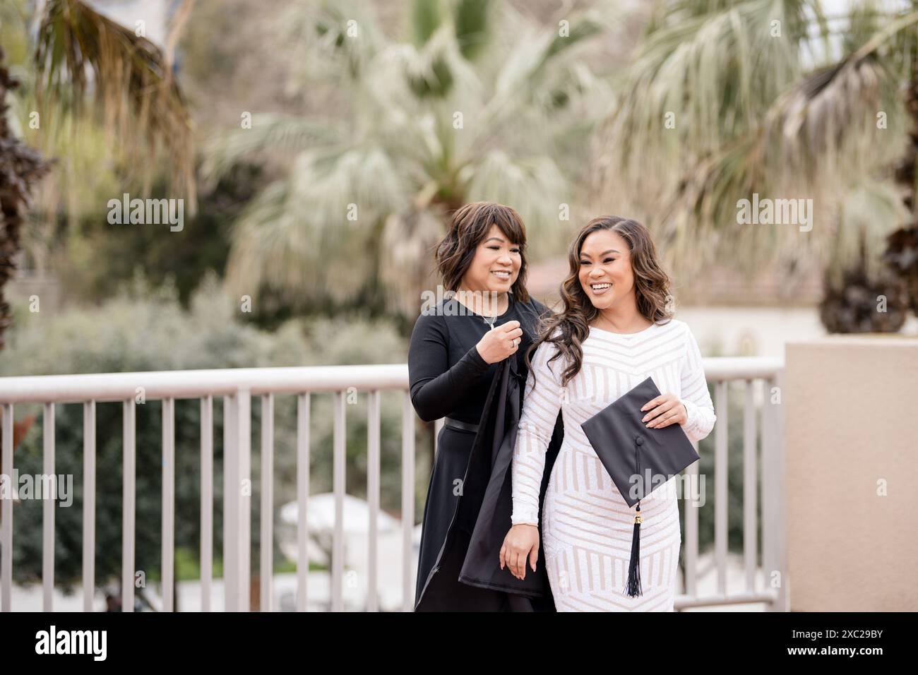 Mom putting graduation gown on daughter both laughing Stock Photo - Alamy