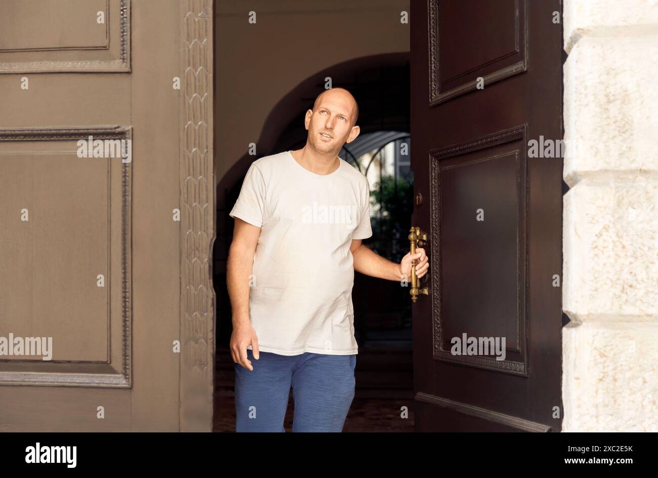 Bald man in white t-shirt holding door at entrance of building Stock ...