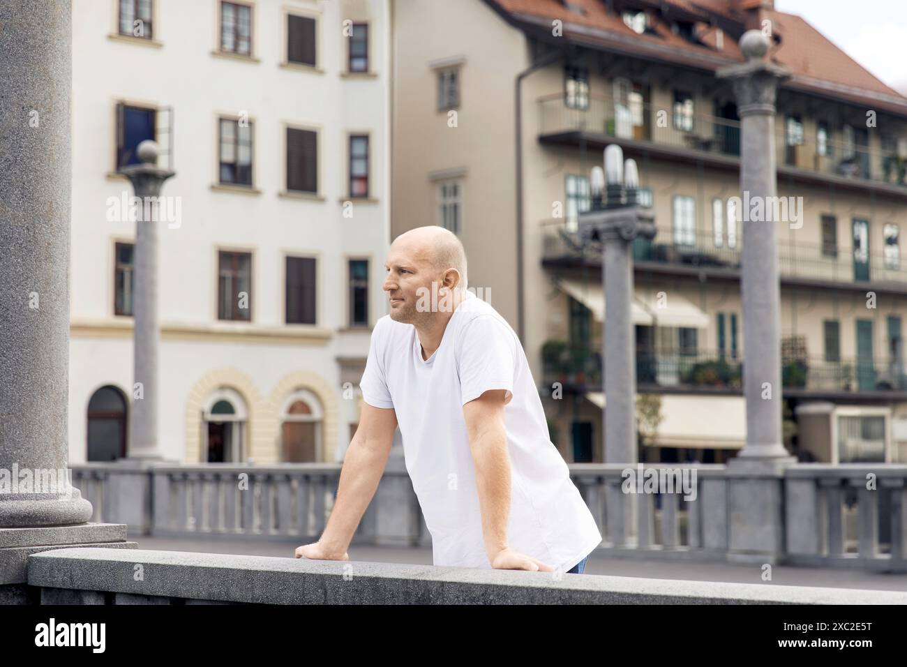 Man in white t-shirt leaning on railing and looking at city buildings ...