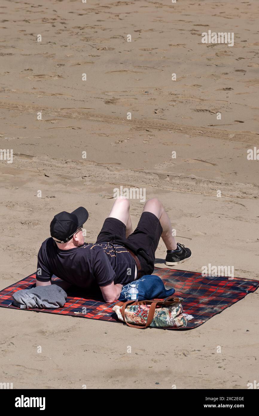 A mature male holidaymaker lying down alone on a blanket on a beach in ...