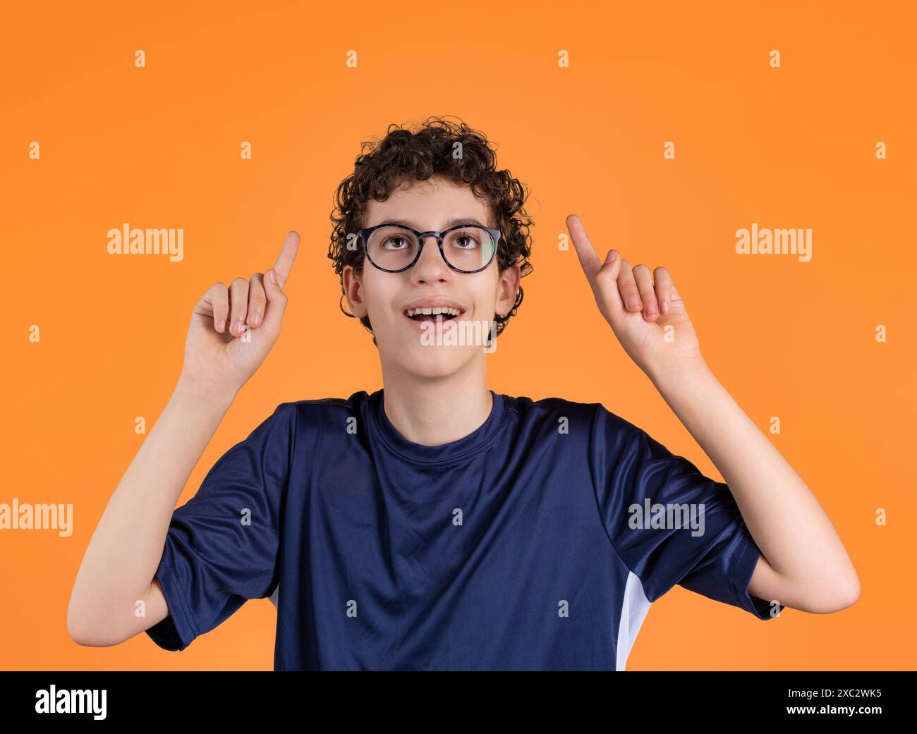 An excited teenage boy with glasses pointing up, smiling, on an orange ...