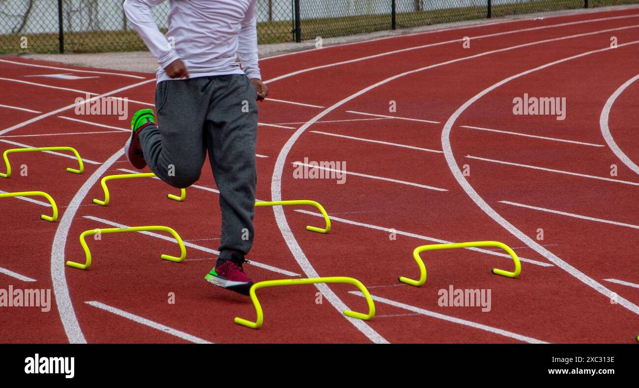 Front view of a high school boy running over small yellow mini hurdles during track practice ...