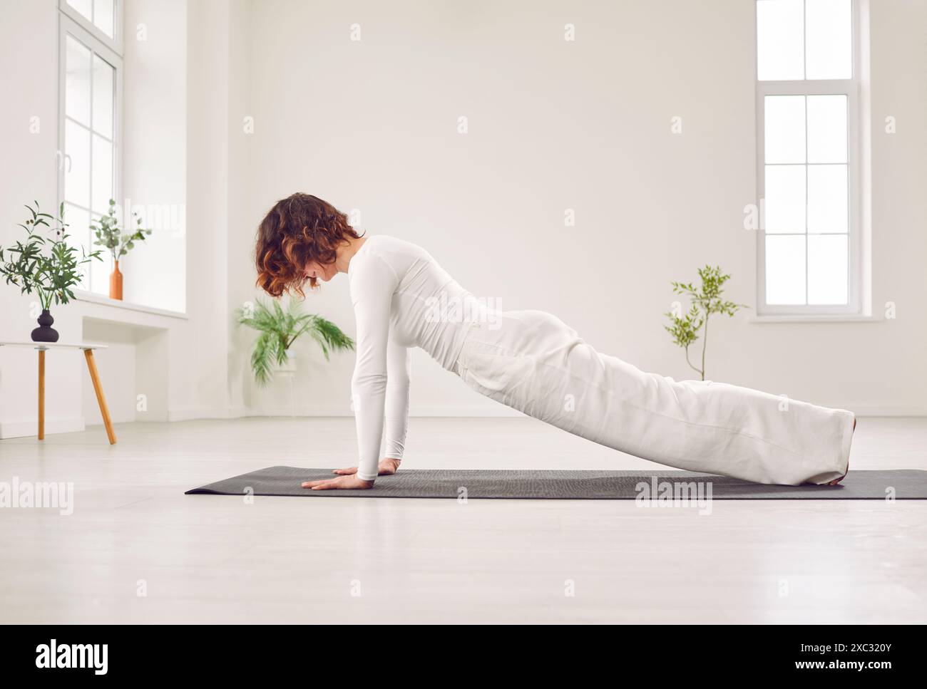 Yogi attractive sporty woman working out in white studio, side view ...