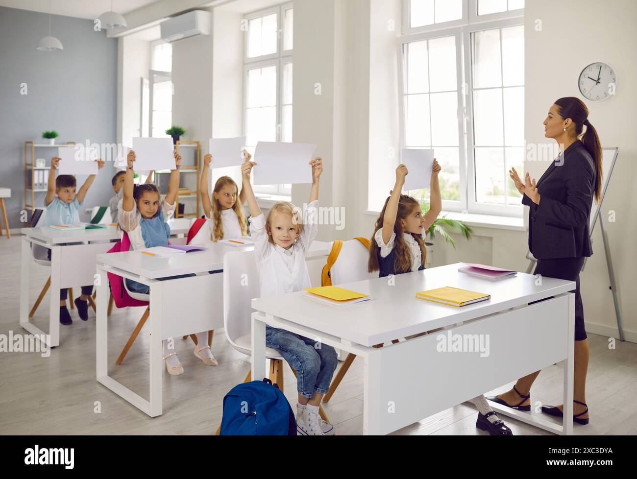 Little children sits in classroom raise sheets of paper during art ...