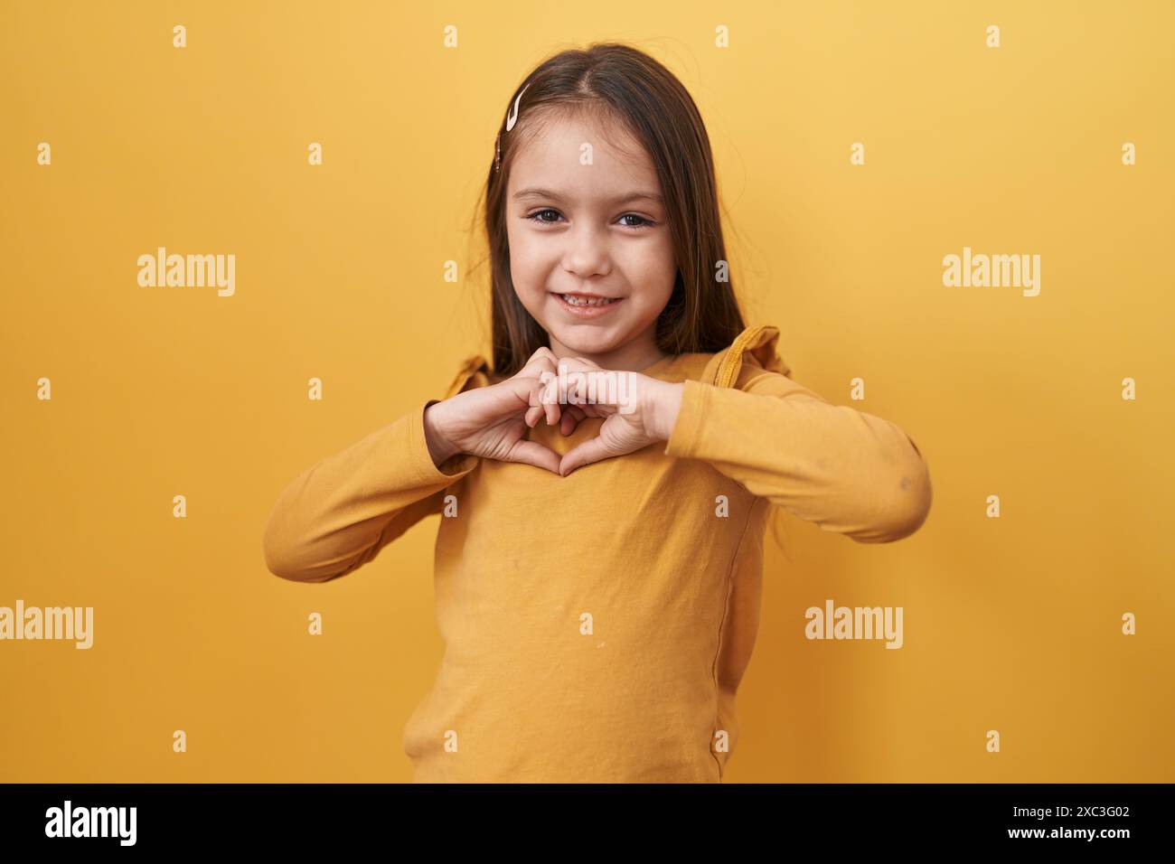 Adorable hispanic girl stands joyfully, her hands shaping an endearing ...