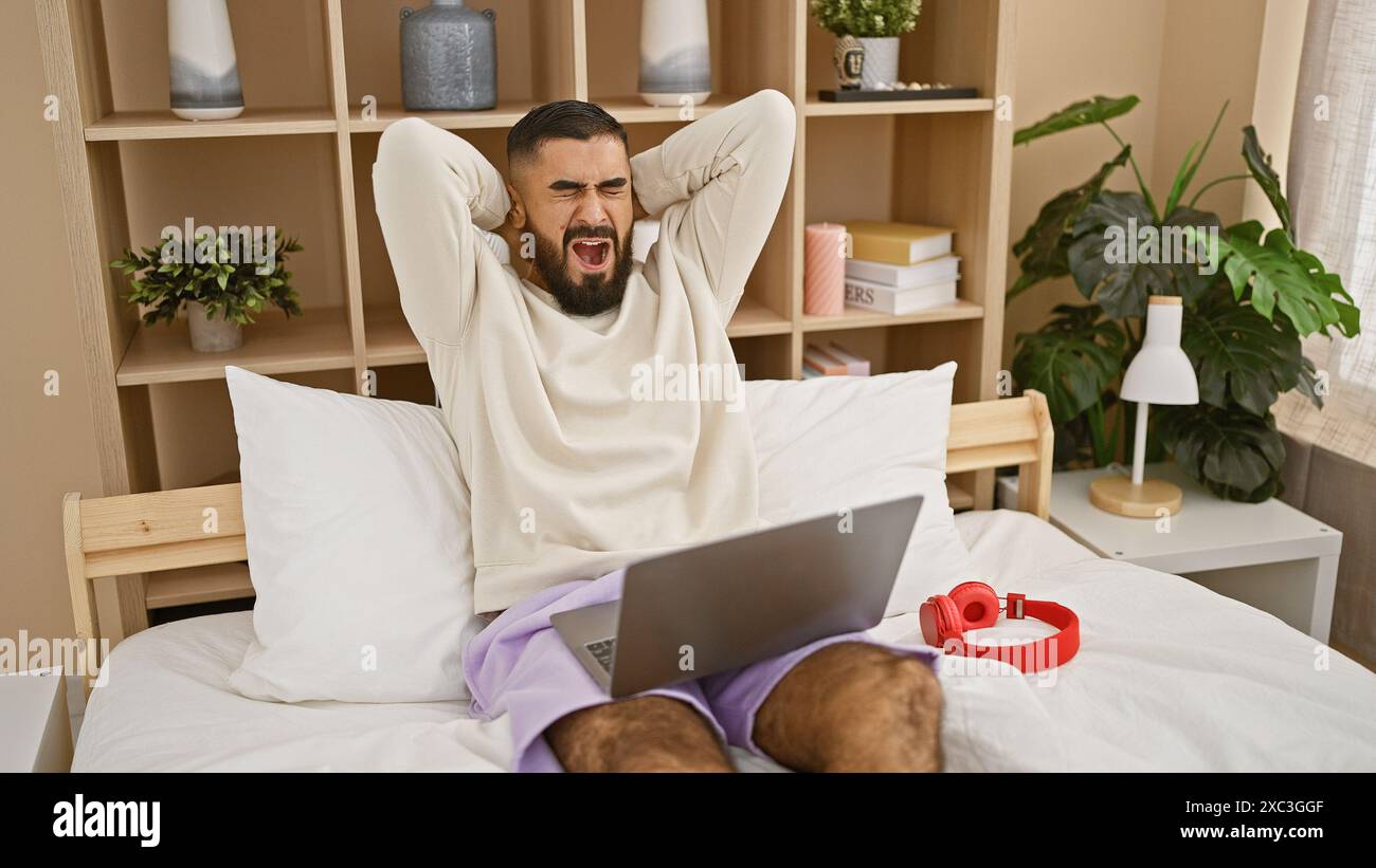 A yawning man with a beard in casual clothing sprawled on bed with ...