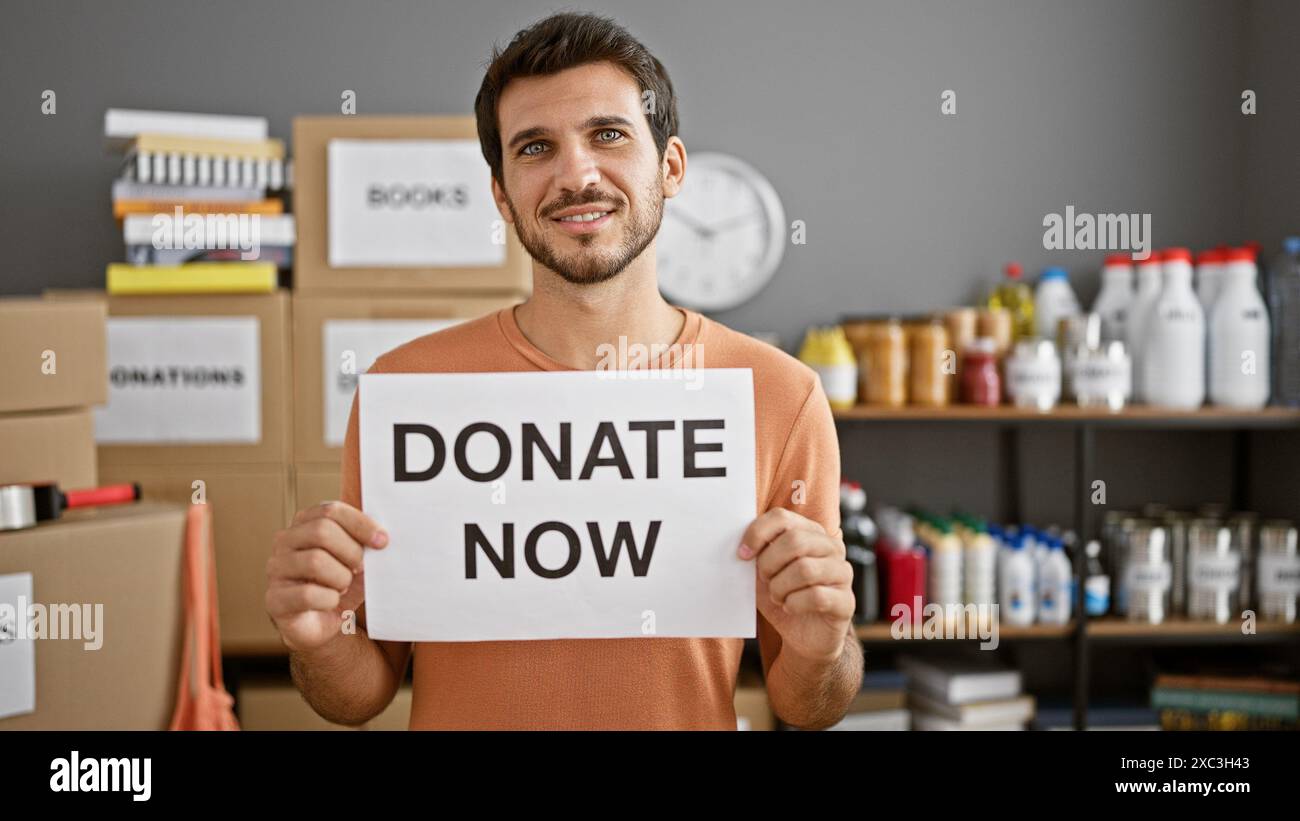 Handsome hispanic man holding 'donate now' sign in a warehouse filled ...